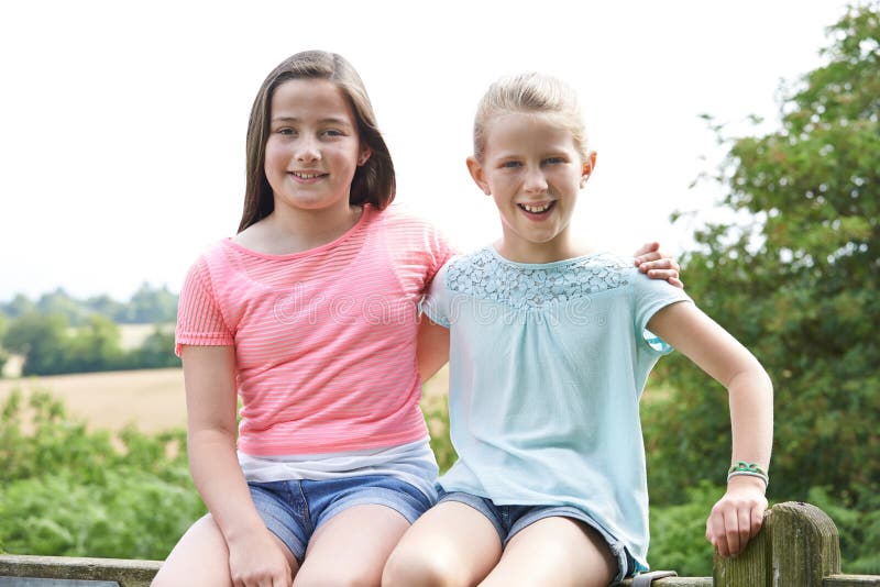 Portrait of Two Girls Sitting on Gate Together Stock Photo - Image of ...