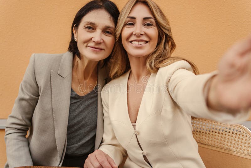 Portrait Of Two Happy Adult Caucasian Girlfriends With Mobile Phones