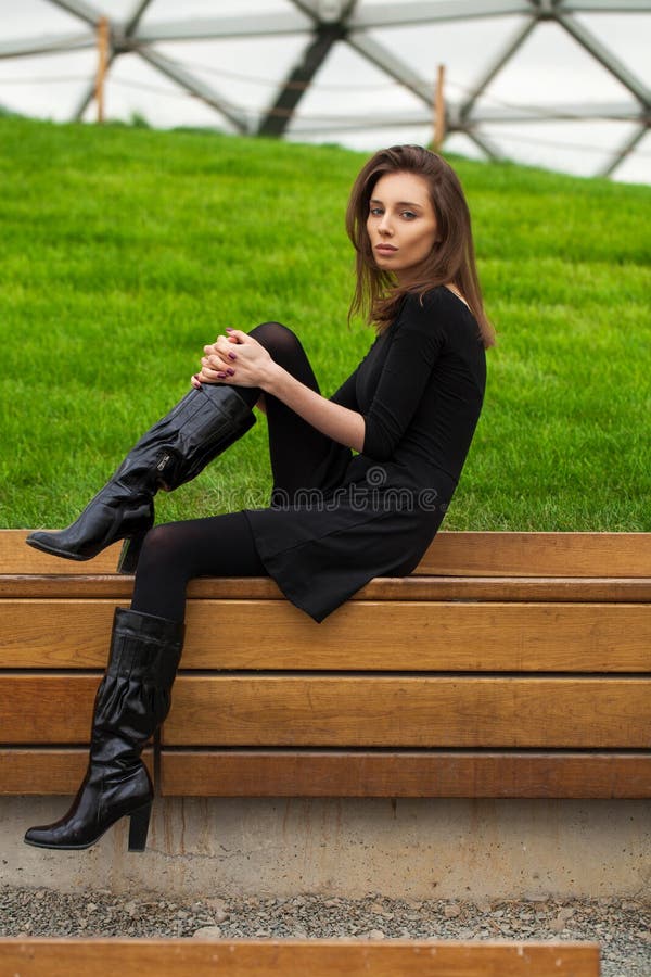 Portrait Of A Young Beautiful Woman In A Black Dress Sitting On The Wooden Bench In The Autumn
