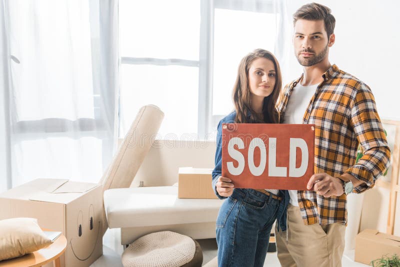 Portrait Of Young Couple Holding Sold Red Card At Home Stock Image