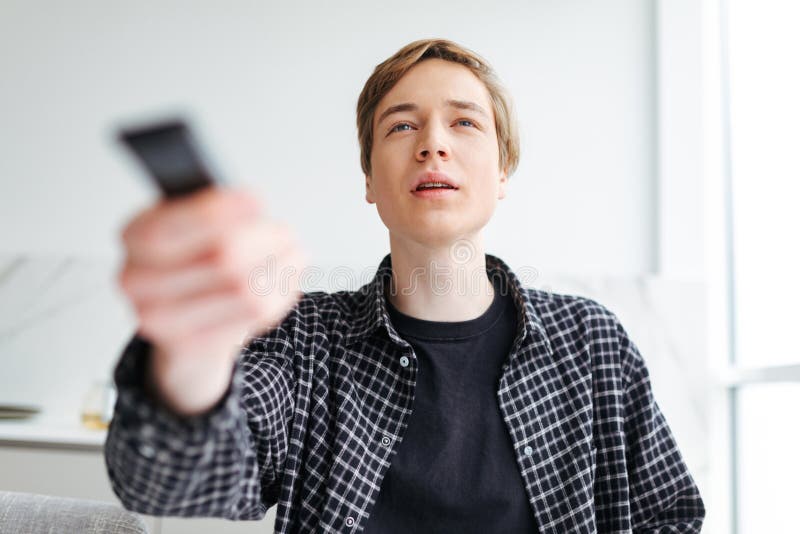 Young Thoughtful Man Using a Remote Control while Watching TV at Home ...