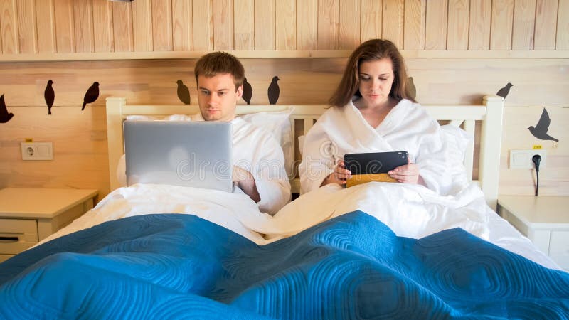 Portrait of Young Very Busy Couple Lying in Bed and Working on Laptop ...