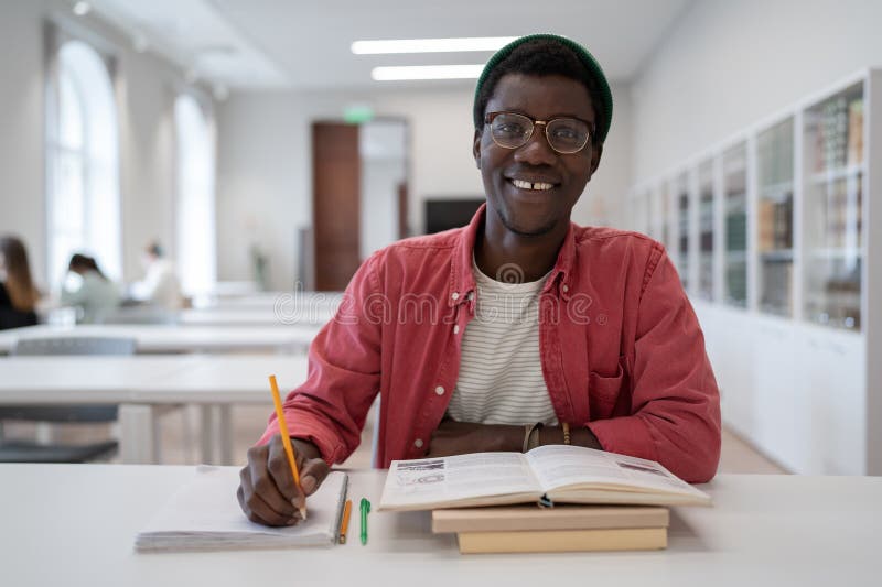 African American Young Man Studying in University Library Making Notes ...
