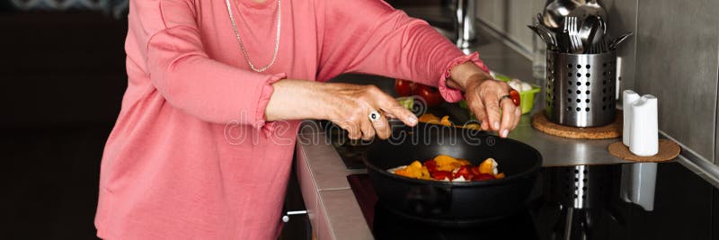 A Positive Elderly Woman Cooking Something on the Stove in the Kitchen ...