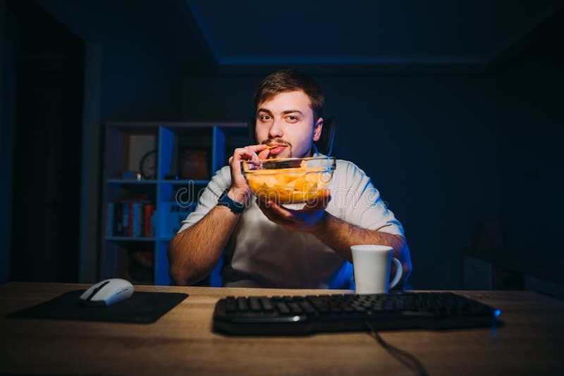 Positive Male Freelancer Works at Night at the Computer and Eats Chips ...