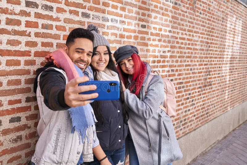 Smiling Multiethnic Friends Taking Selfie On Smartphone Near Brick Wall