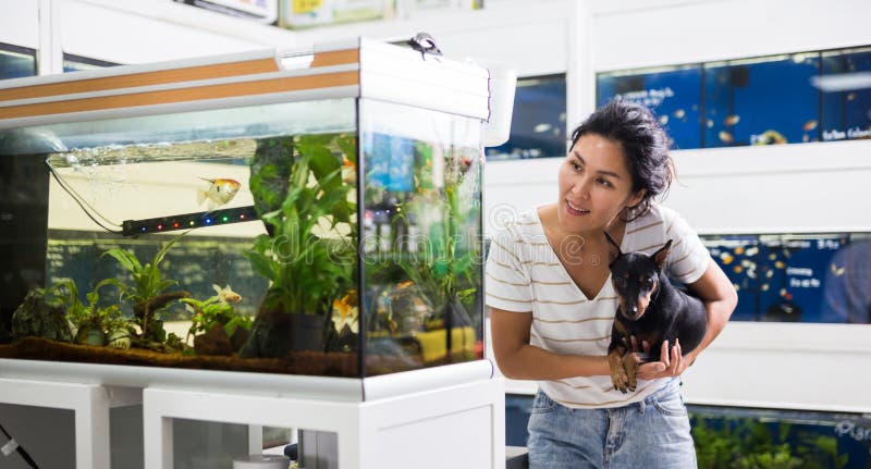 Positive Woman with Dog in Her Arms Choosing Aquarium Fish at Pet Shop ... Positive Woman with Dog in Her Arms Choosing Aquarium Fish at Pet Shop ...