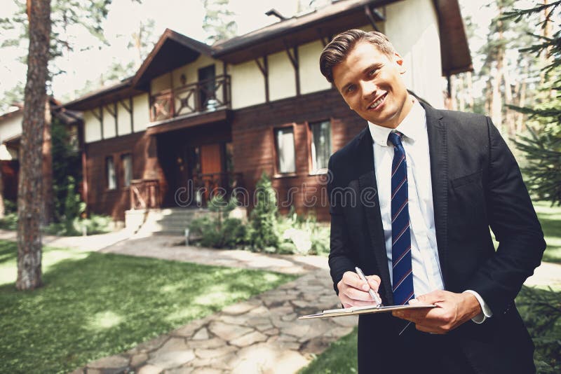Positive Young Realtor Making Notes while Standing in Front of the ...
