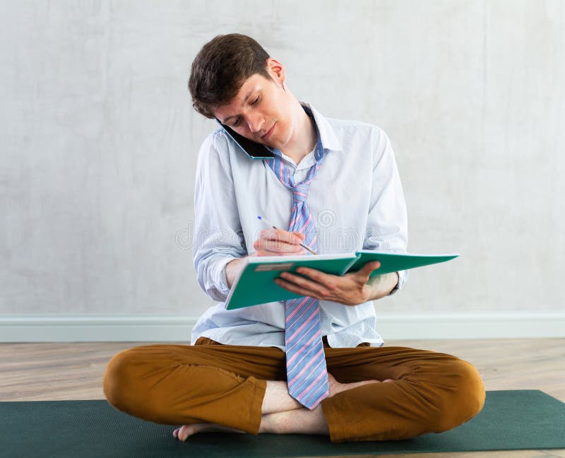 Positive Young Student Talking on a Mobile Phone and Making Notes in ...