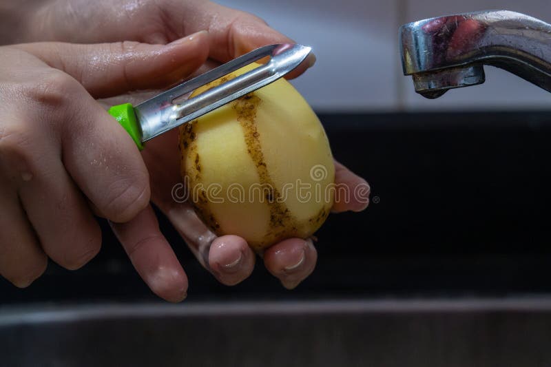 Potapo Peeling. Hands Peeling Raw Potato with Vegetable Peeler in the ...