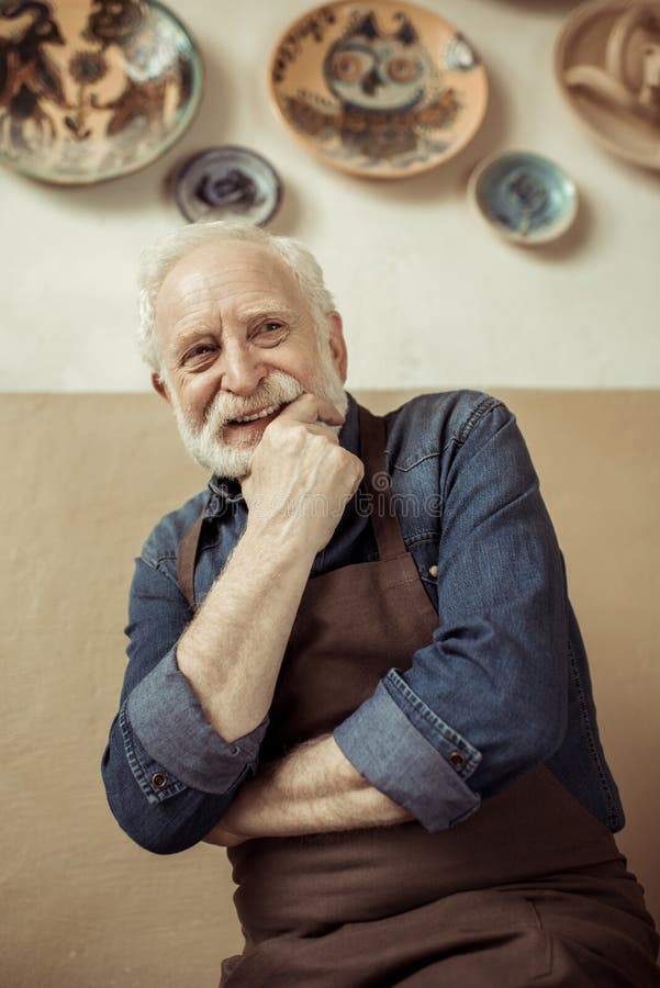 Potter in Apron Thinking and Standing Against Wall with Hanging Pottery ...