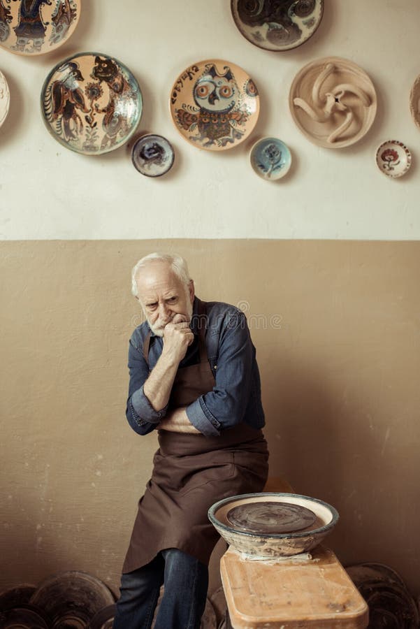 Potter in Apron Thinking and Standing Against Wall with Hanging Pottery ...