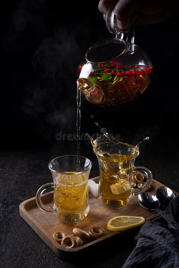 Pour Black Tea from a Transparent Teapot into a Cup on Black Backround ...