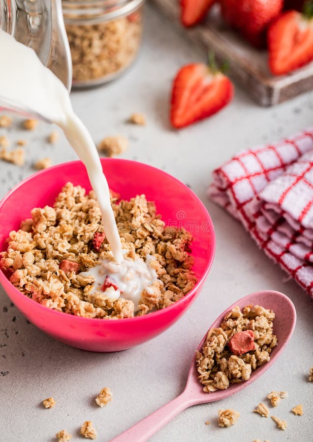 Pouring Milk into Bowl with Strawberry Granola on Light Kitchen Board ...
