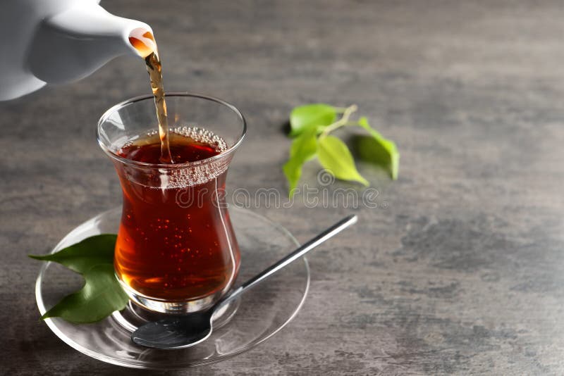 Pouring Traditional Turkish Tea from Pot into Glass on Grey Table ...