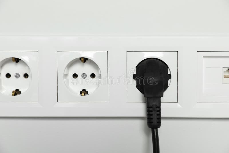 Power Sockets with Inserted Plug on White Wall, Closeup. Electrical ...