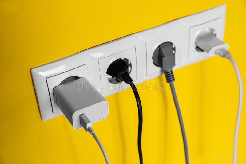 Power Sockets with Inserted Plugs on Yellow Wall, Closeup. Electrical ...