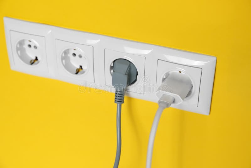 Power Sockets with Inserted Plugs on Yellow Wall, Closeup. Electrical ...