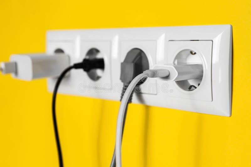 Power Sockets with Inserted Plugs on Yellow Wall, Closeup. Electrical ...