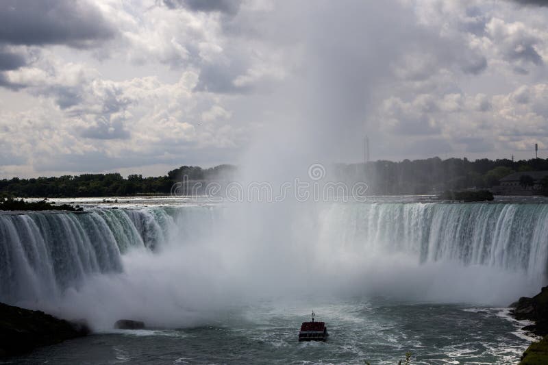 A Powerful Horseshoe Waterfall Creates Mist while a Boat Approaches in ...