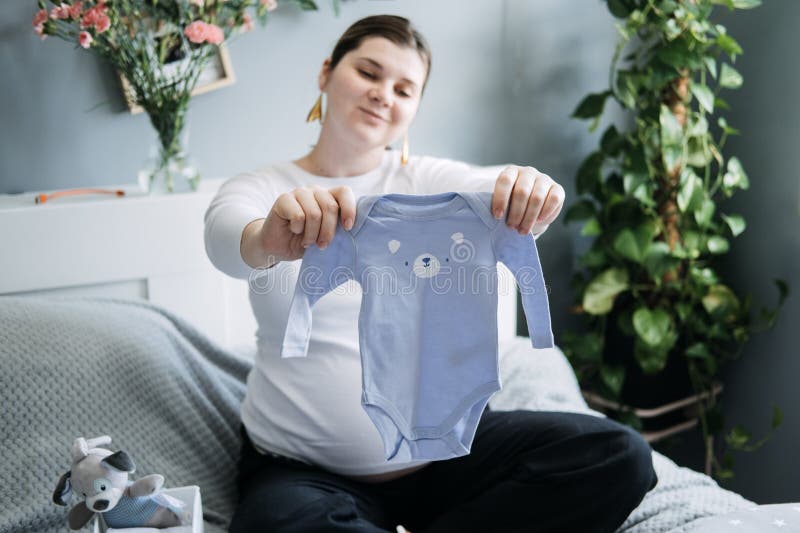 Pregnant Woman With Big Belly Holding Bodysuit And Sorting Clothes For