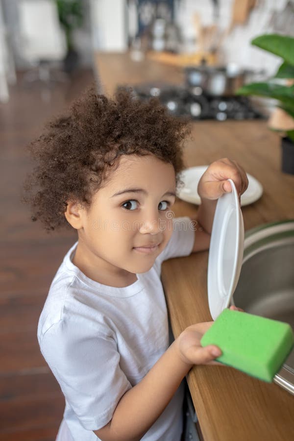 Pretty Curly-haired Kid Holding a Plate and a Sponge in Her Hands Stock ...