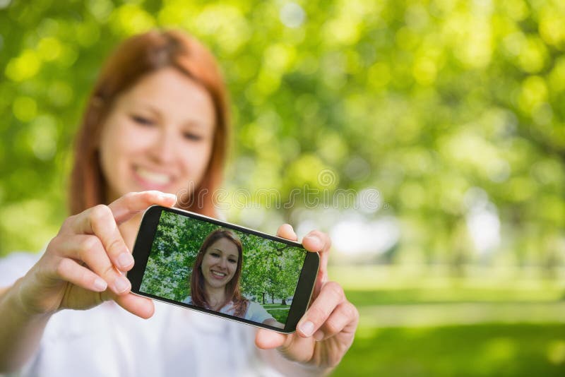 Pretty Redhead Taking A Selfie On Her Phone In The Park Stock Image
