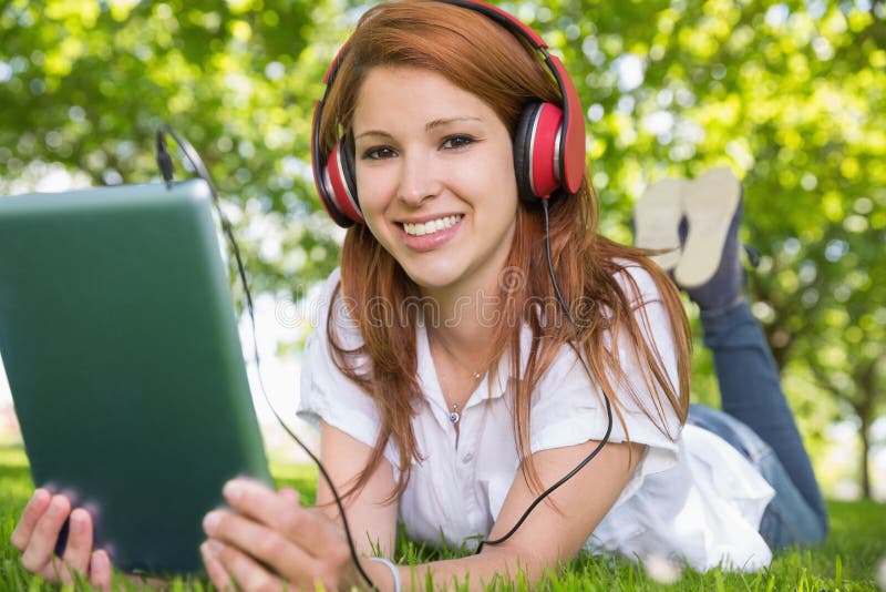 Pretty Redhead Using Her Tablet Pc While Listening To Music In The Park