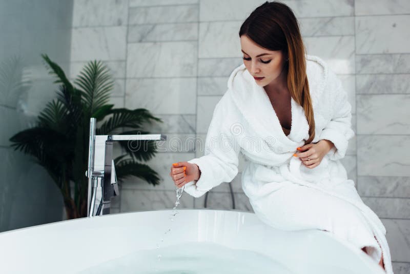 Pretty Slim Woman Wearing Bathrobe Sitting on Edge of Bathtub Filling ... Pretty Slim Woman Wearing Bathrobe Sitting on Edge of Bathtub Filling ...
