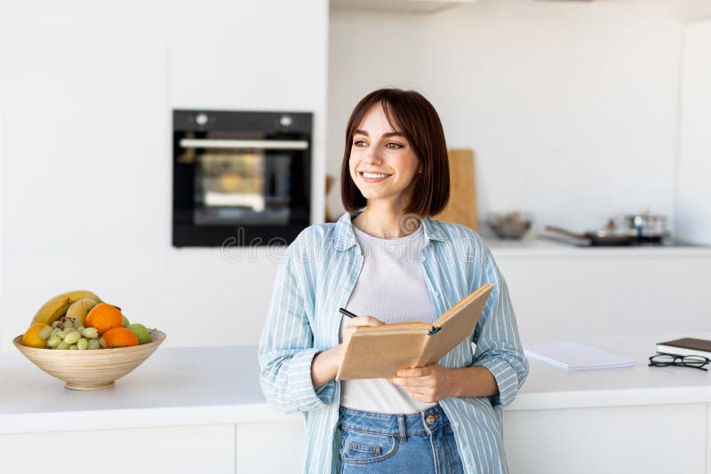 Pretty Woman Taking Notes, Holding Notepad and Pen, Standing in Kitchen ...