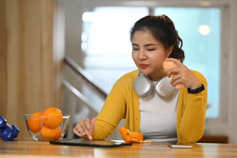 Pretty Young Woman Eating an Orange and Using a Digital Tablet on ...