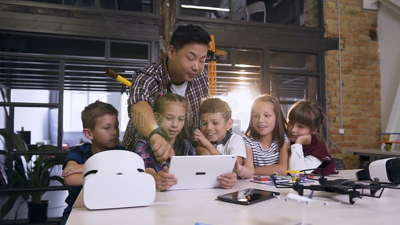 Primary School Teacher at Desk Working with Five Young Pupils Using ...