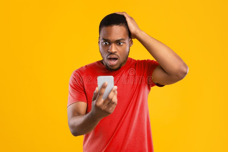 Concerned Black Guy Looking at Cellphone in Shock, Yellow Background ...