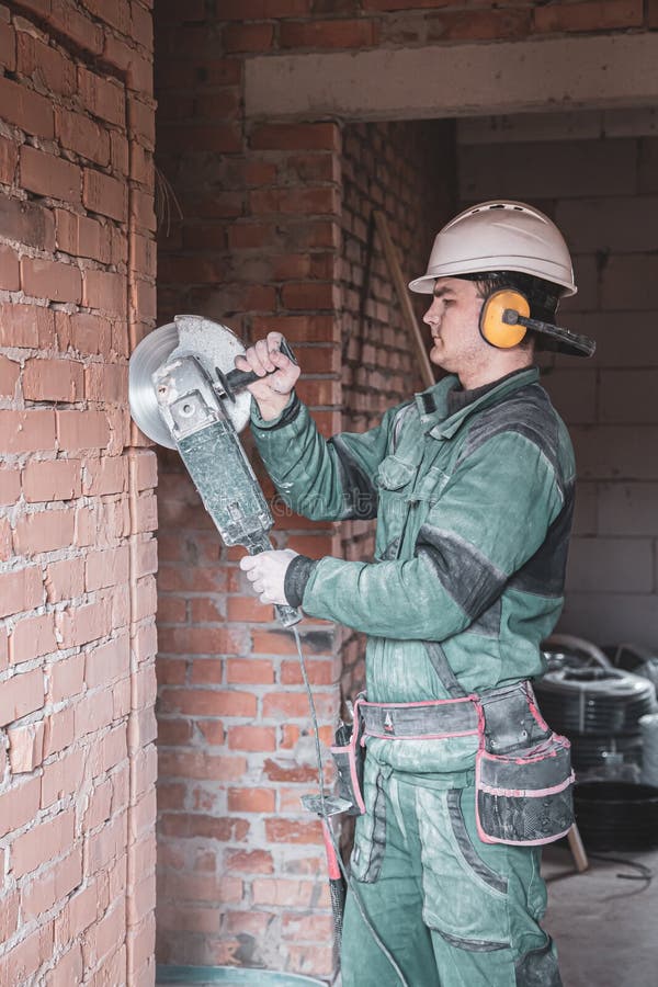 A Professional Builder in Work Clothes Works with a Cutting Tool Stock ...