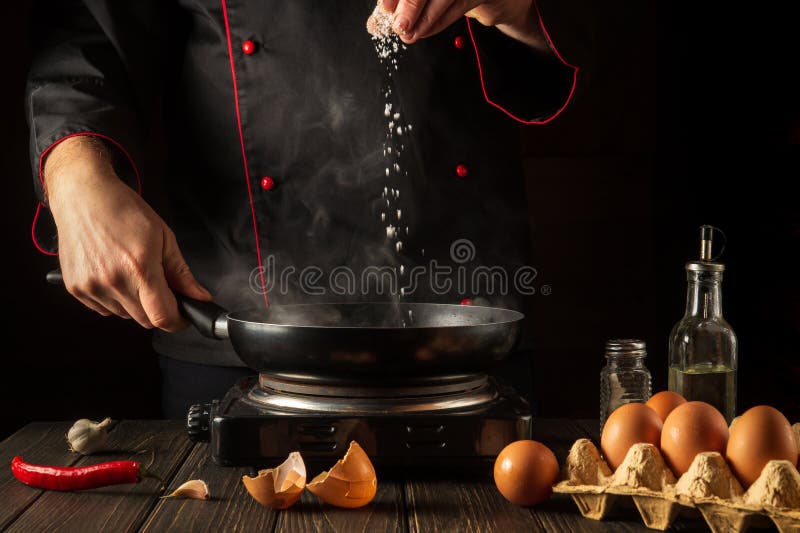 Professional Chef Adds Salt while Cooking Eggs in Pan. Work Environment ...