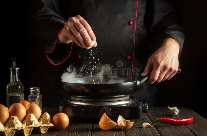 Professional Chef Adds Salt while Cooking Eggs in Pan. Work Environment ...