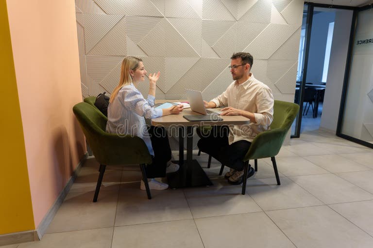 Two Colleagues Discussing Work while Seated at a Modern Office Table ...