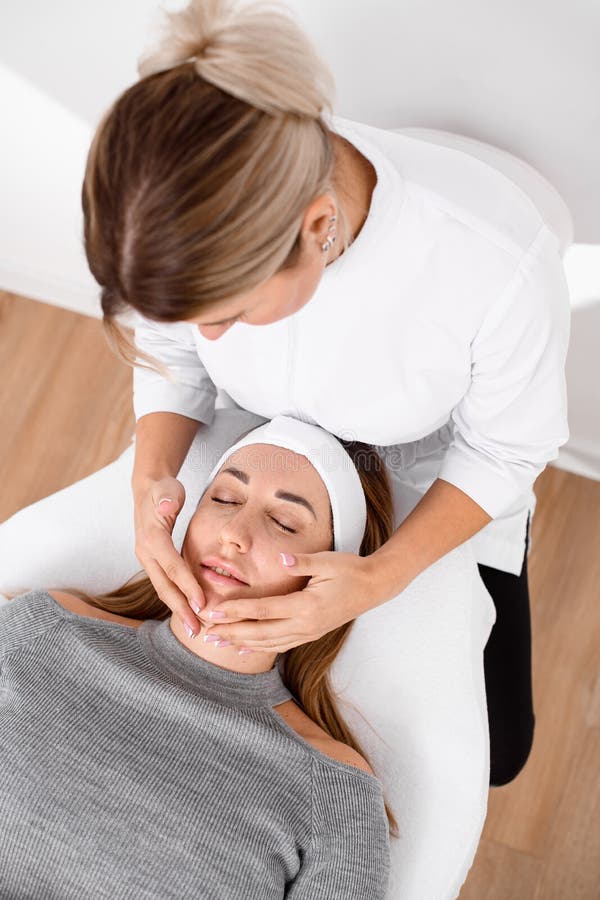Professional Cosmetologist Doing Face Massage To Woman At Beauty Salon