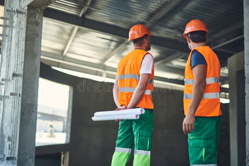 Two Builders in Uniform Looking at the Unfinished Building Stock Photo ...
