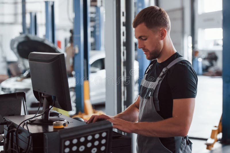 Professional Mechanic. Man at the Workshop in Uniform Use Computer for ...