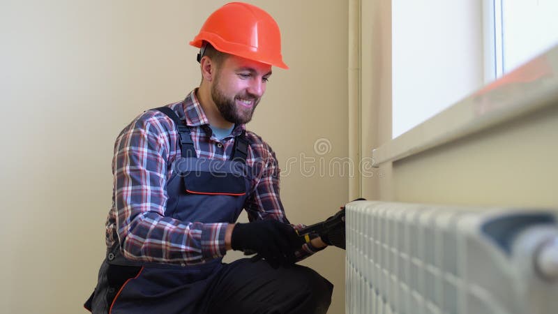 Professional Plumber in a Hard Hat and Gloves Installing Radiator in a ...