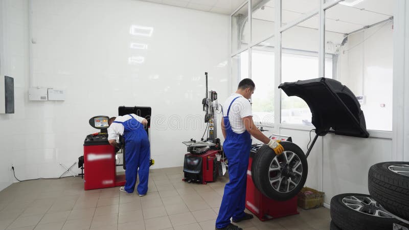 Auto Mechanics in Uniform Work in Tire Shop with Equipment. Professional Servicing Car Wheel ...