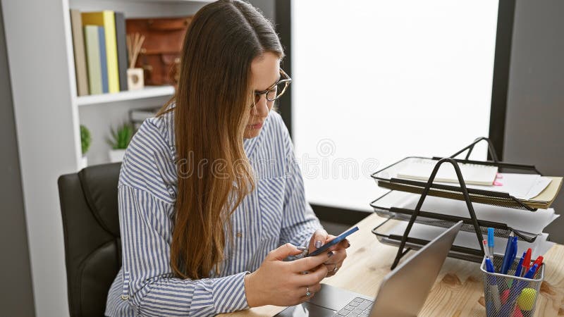 A Professional Woman Multitasks in a Modern Office, Using a Smartphone ...