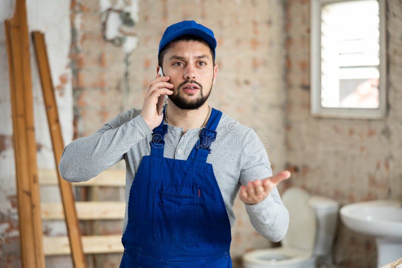 Professional Worker in Blue Overalls Speaks on a Mobile Phone in ...
