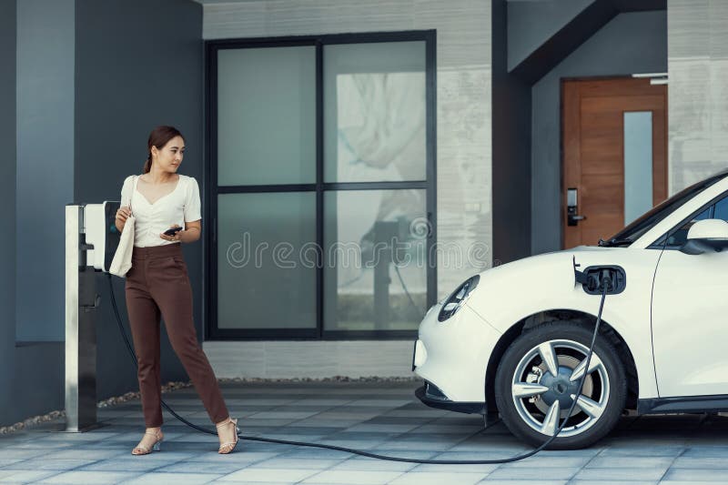Progressive Woman Holding Phone at EV Home Charging Station in Garage ... Progressive Woman Holding Phone at EV Home Charging Station in Garage ...