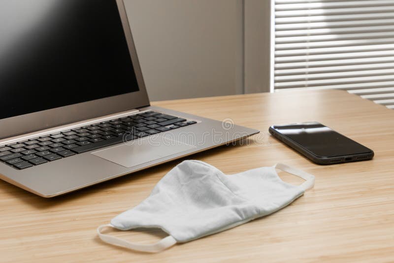 A Protective Mask, Smartphone and a Laptop are on the Desk ...