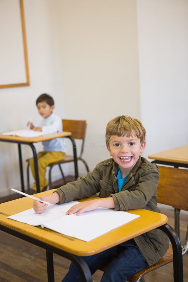 Pupil Writing in Notepad at His Desk Smiling at Camera Stock Photo ...