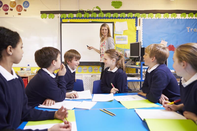 Pupils Sitting at Table As Teacher Stands by Whiteboard Stock Image ...