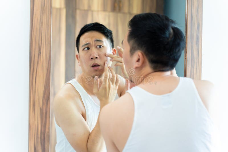 Puzzled Asian Man Checking Acne Problems while Looking in Mirror Stock ...