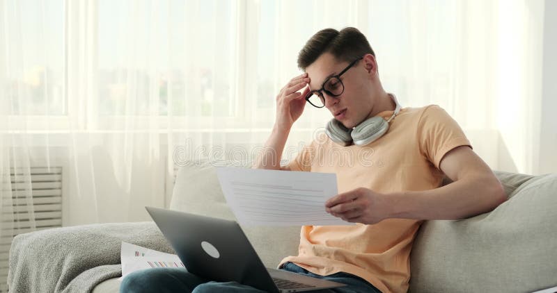 Puzzled Man Working with Documents and Laptop while Sitting on Sofa ...